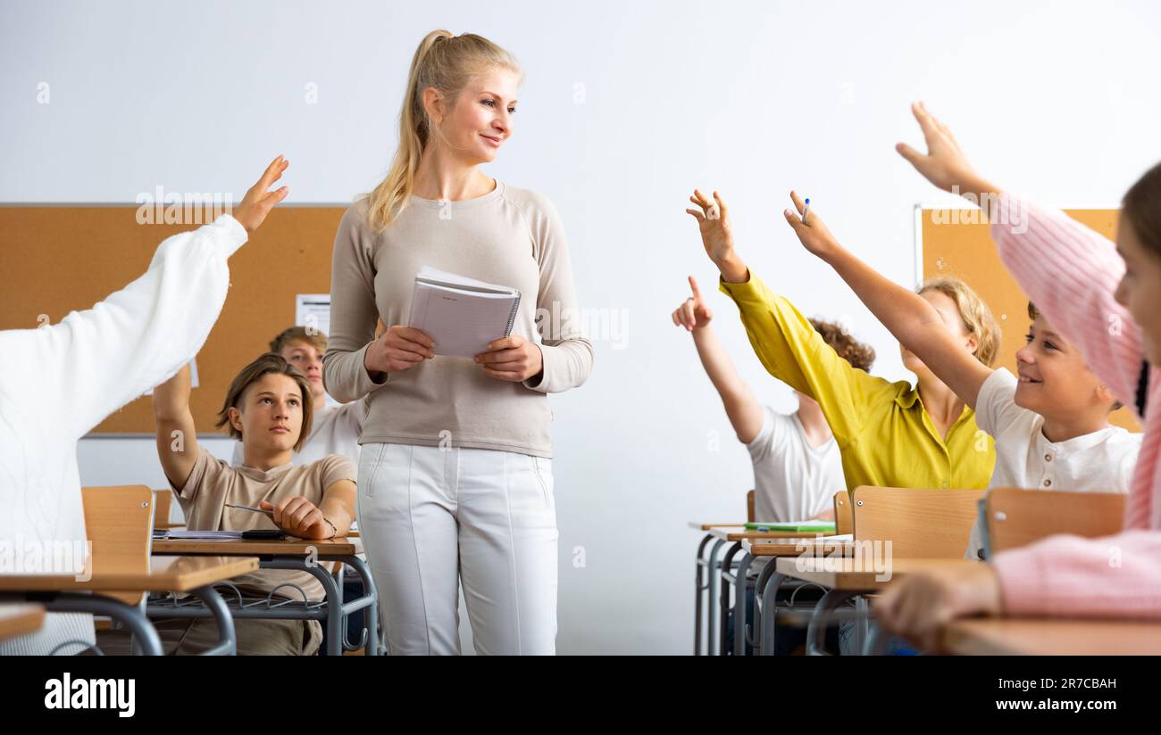 Female teacher lecturing in classroom and kids raising hands Stock ...