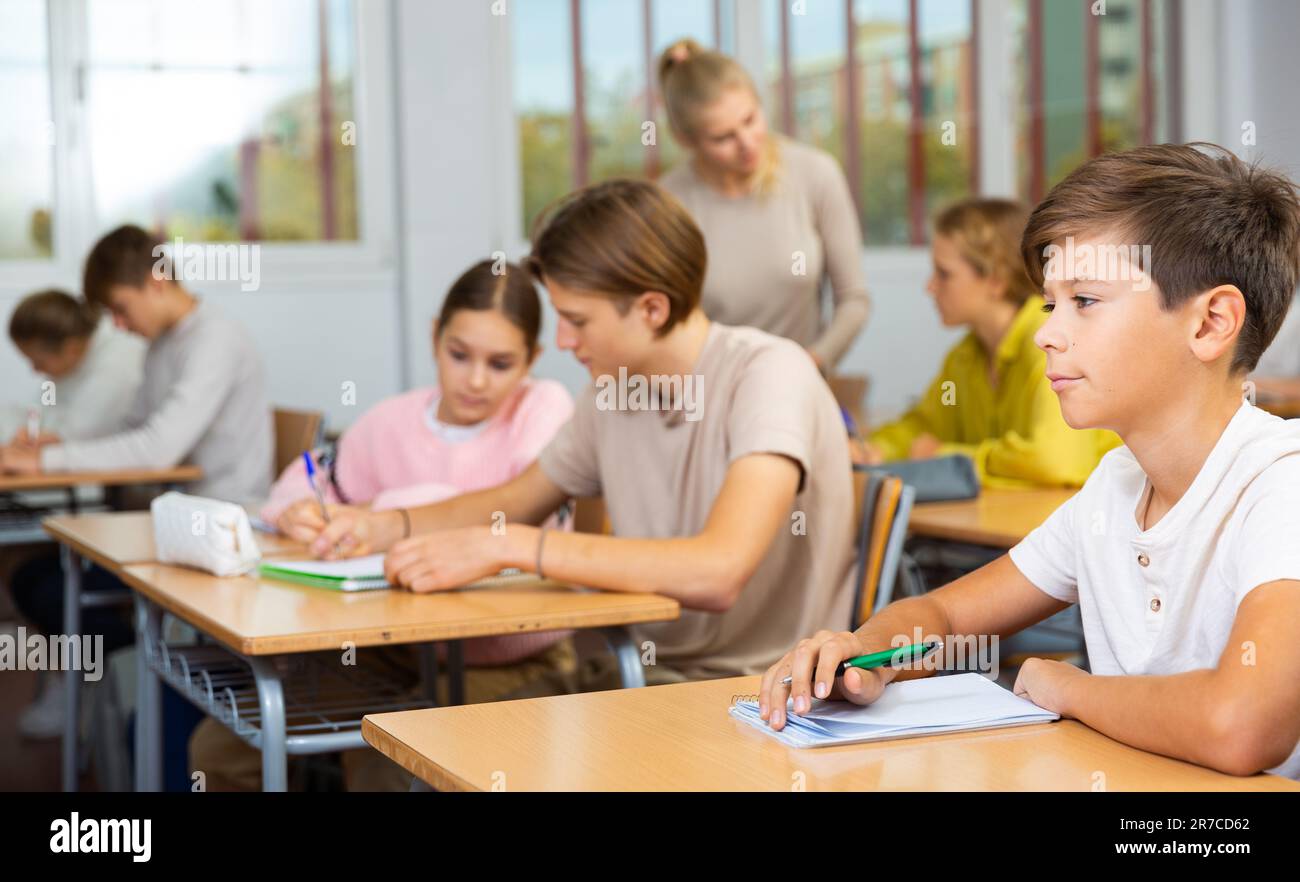 Boy listening to lecturer and writing in notebook in classroom Stock ...