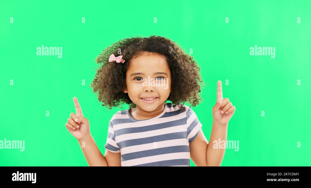 Face smile, girl child and pointing up on green screen in studio ...