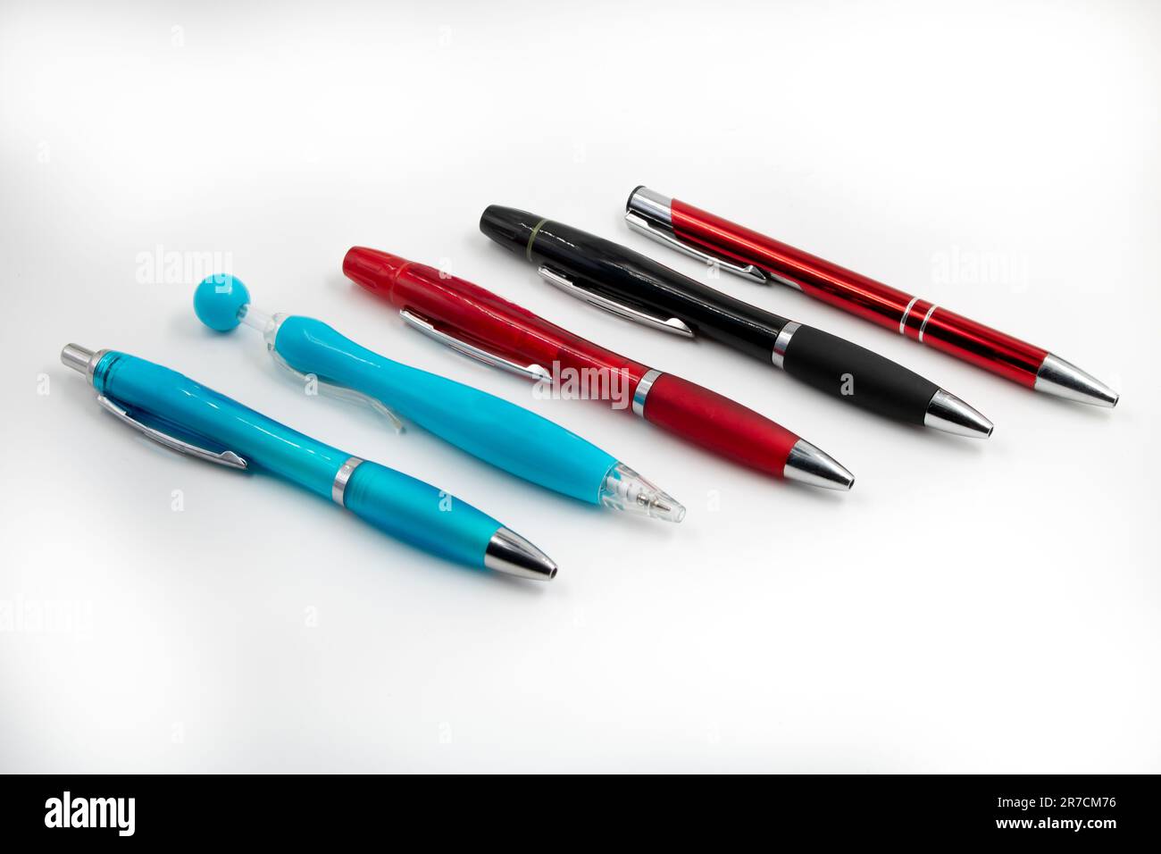 A set of different colored pens resting on a solid white background ...