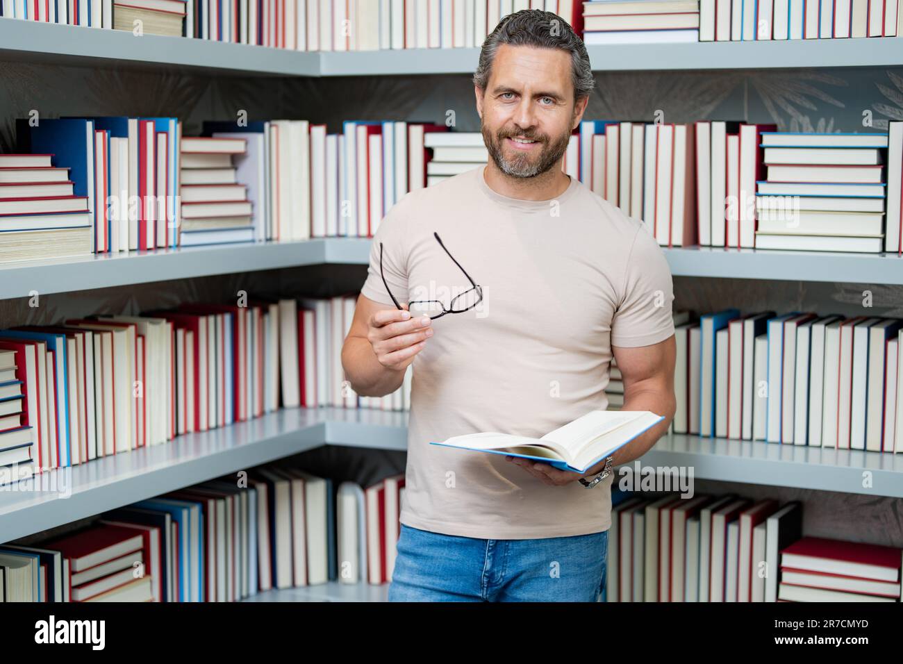 Portrait of teacher with book in library classroom. Handsome teacher in ...