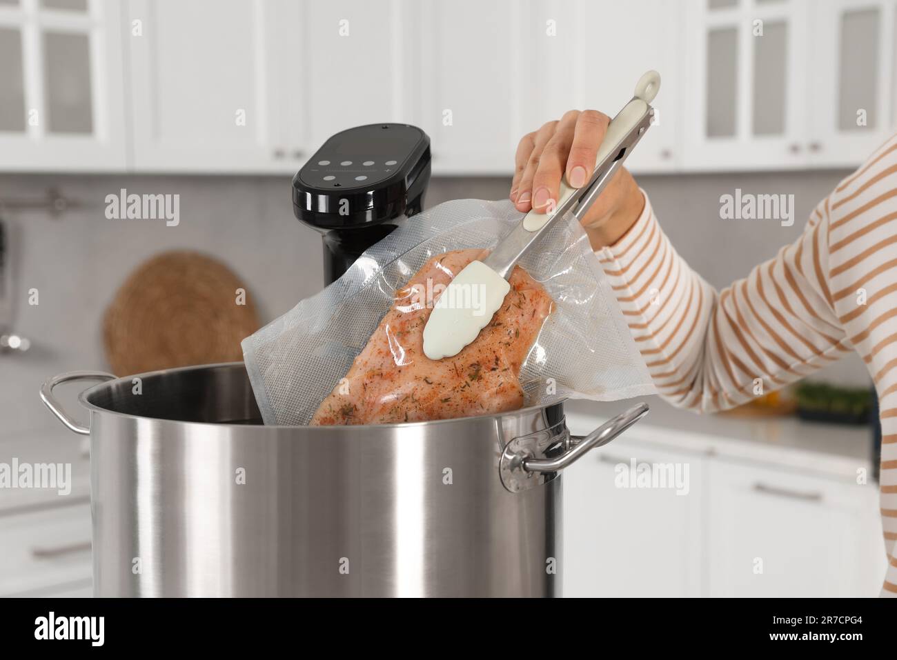 Woman putting vacuum packed meat into pot with sous vide cooker in ...