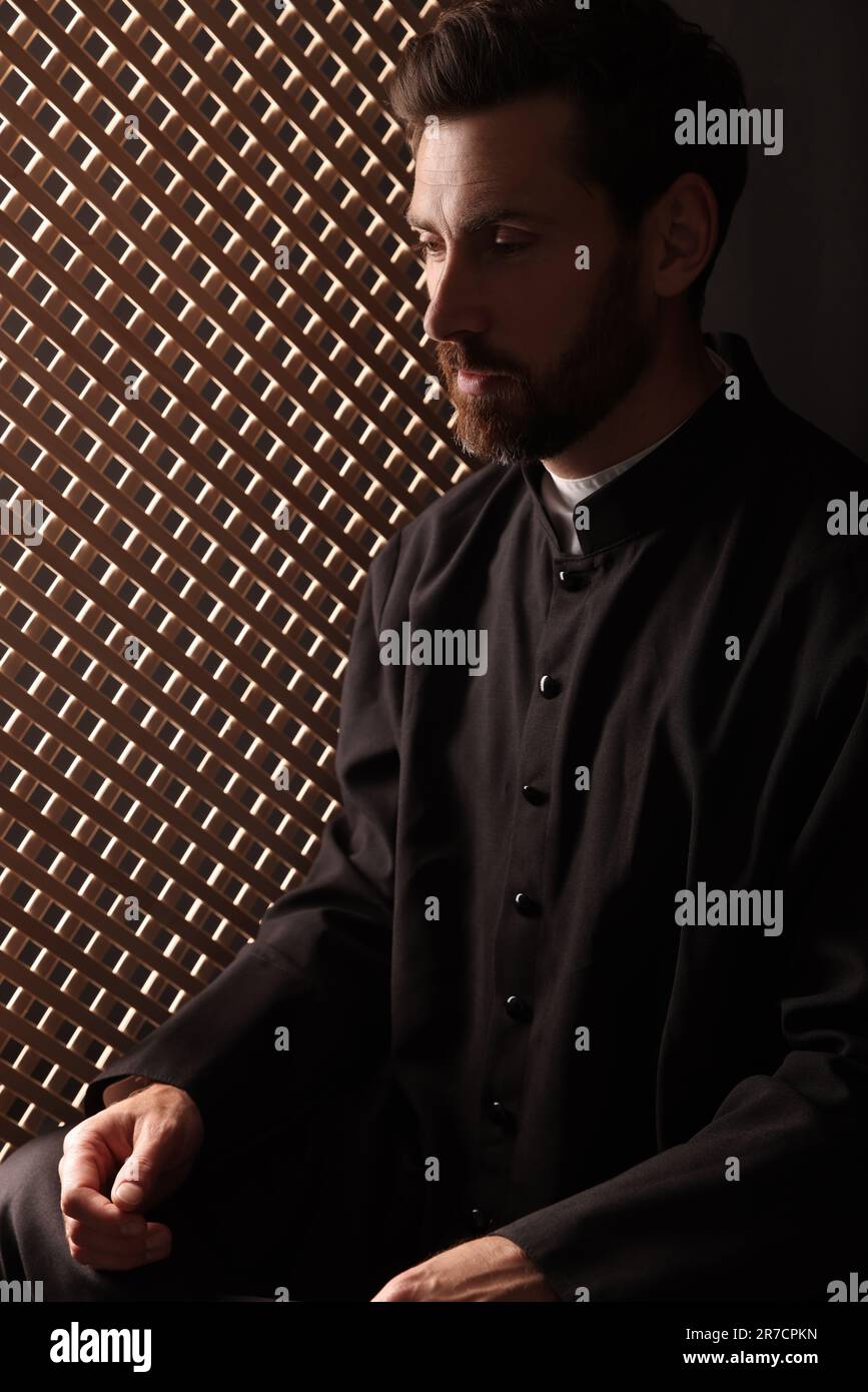Catholic priest wearing cassock in confessional booth Stock Photo - Alamy