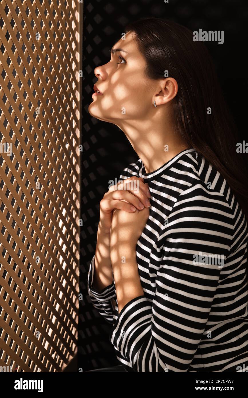 Woman listening to priest during confession near wooden partition in ...