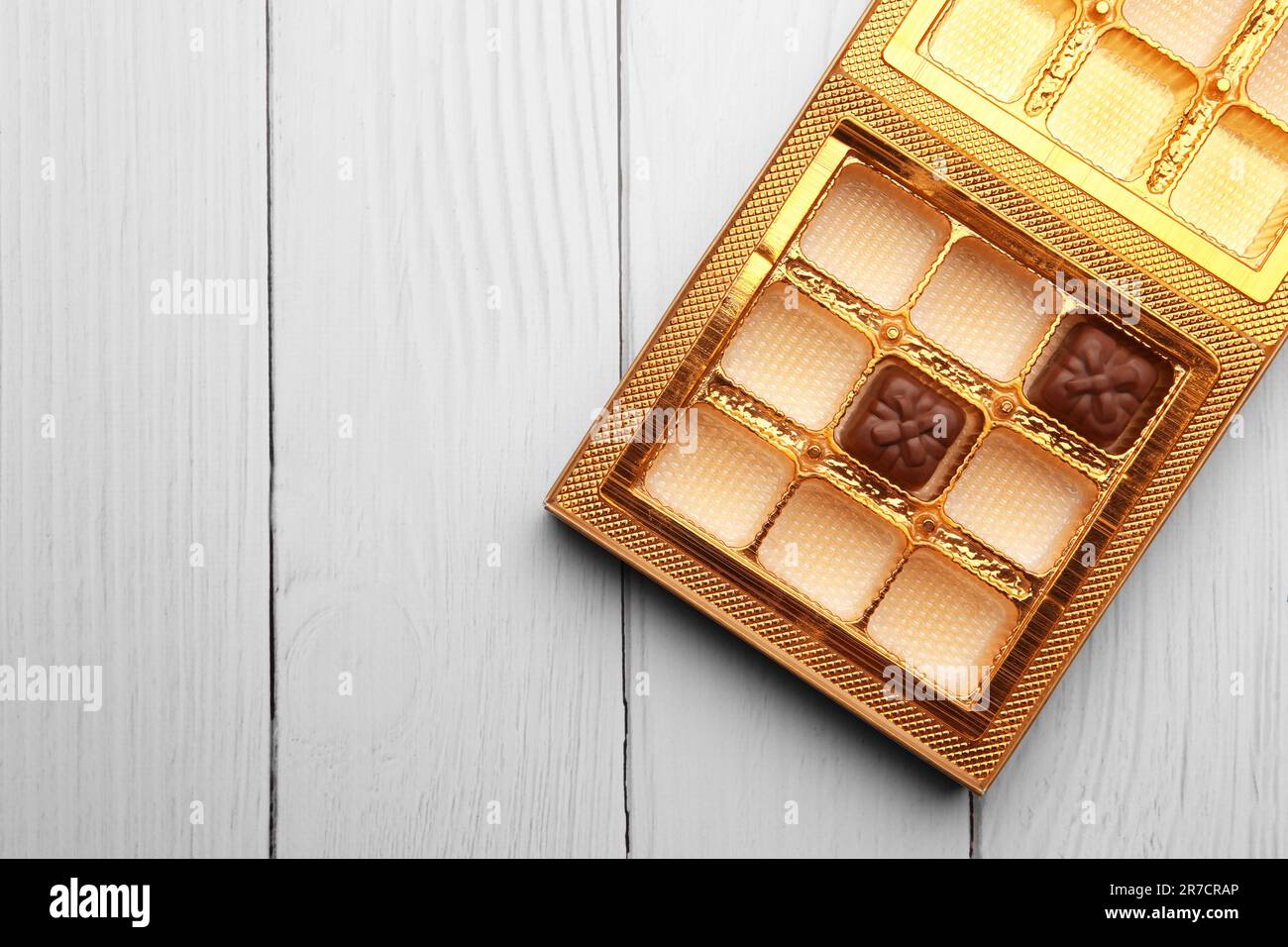 Partially empty box of chocolate candies on white wooden table, top ...