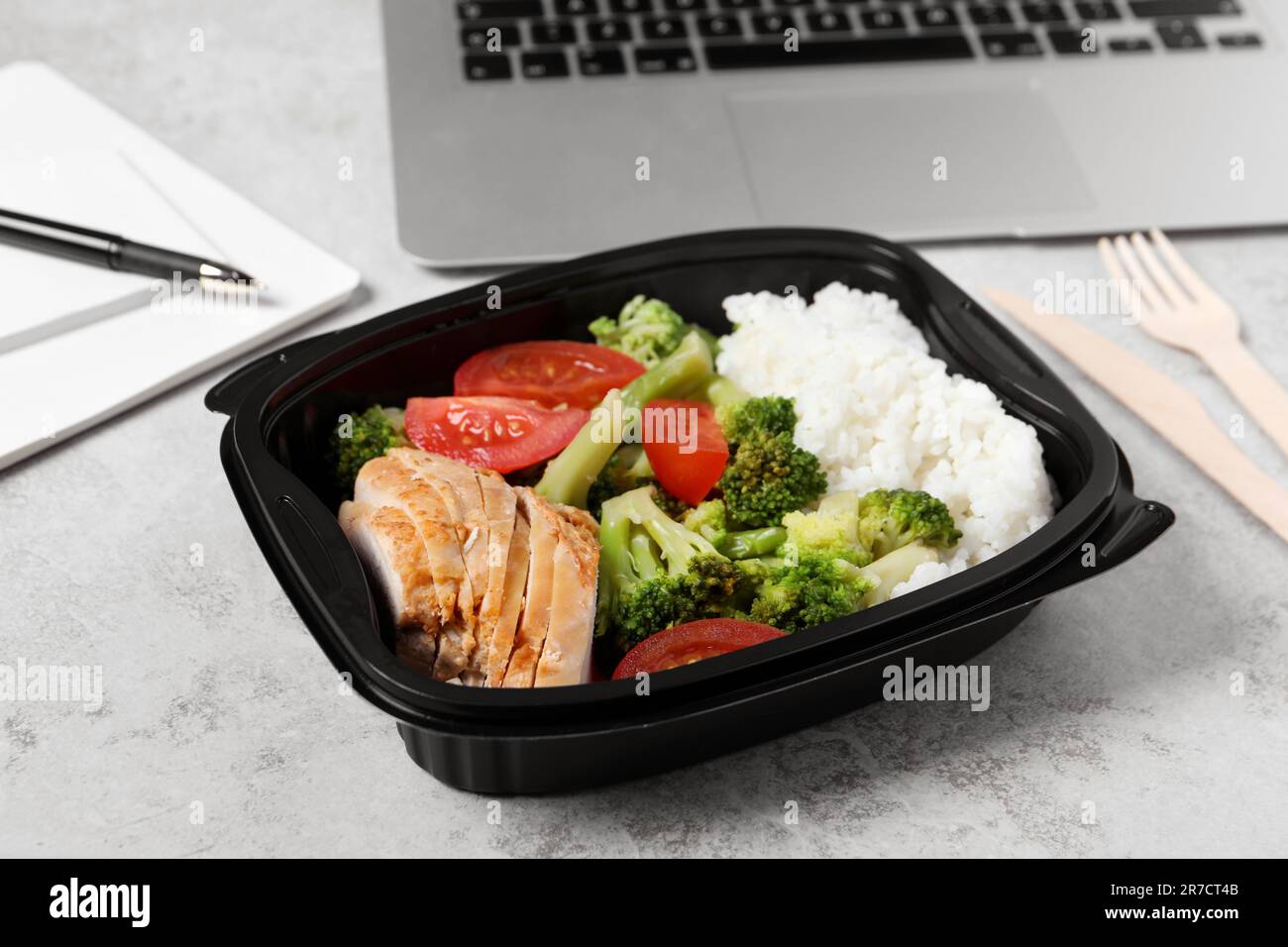 Container with tasty food, laptop, cutlery and notebook on light grey ...