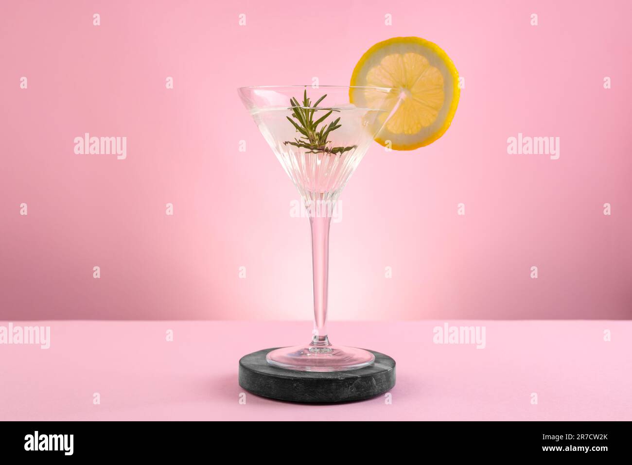 Martini glass of cocktail with lemon slice and rosemary on stand ...