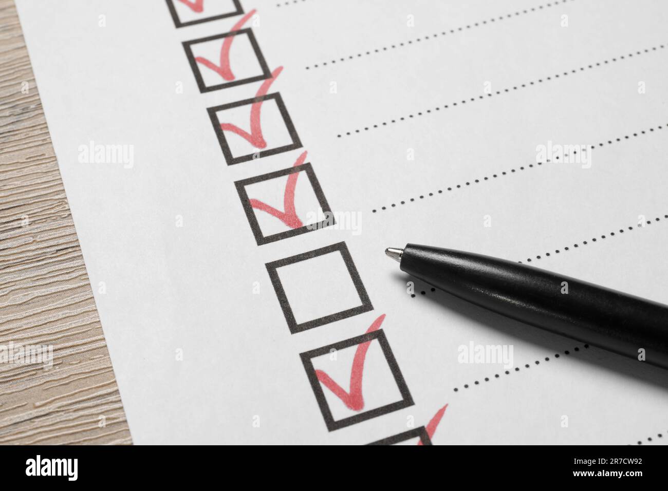 Paper sheet with checkboxes and pen on wooden table, closeup. Checklist ...