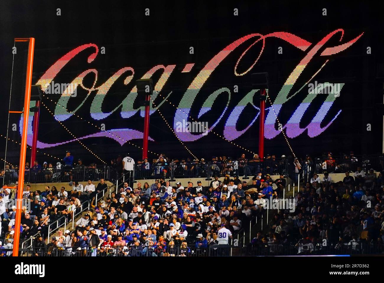 Fans sit in front of a rainbow-colored Coca-Cola sign during the ...