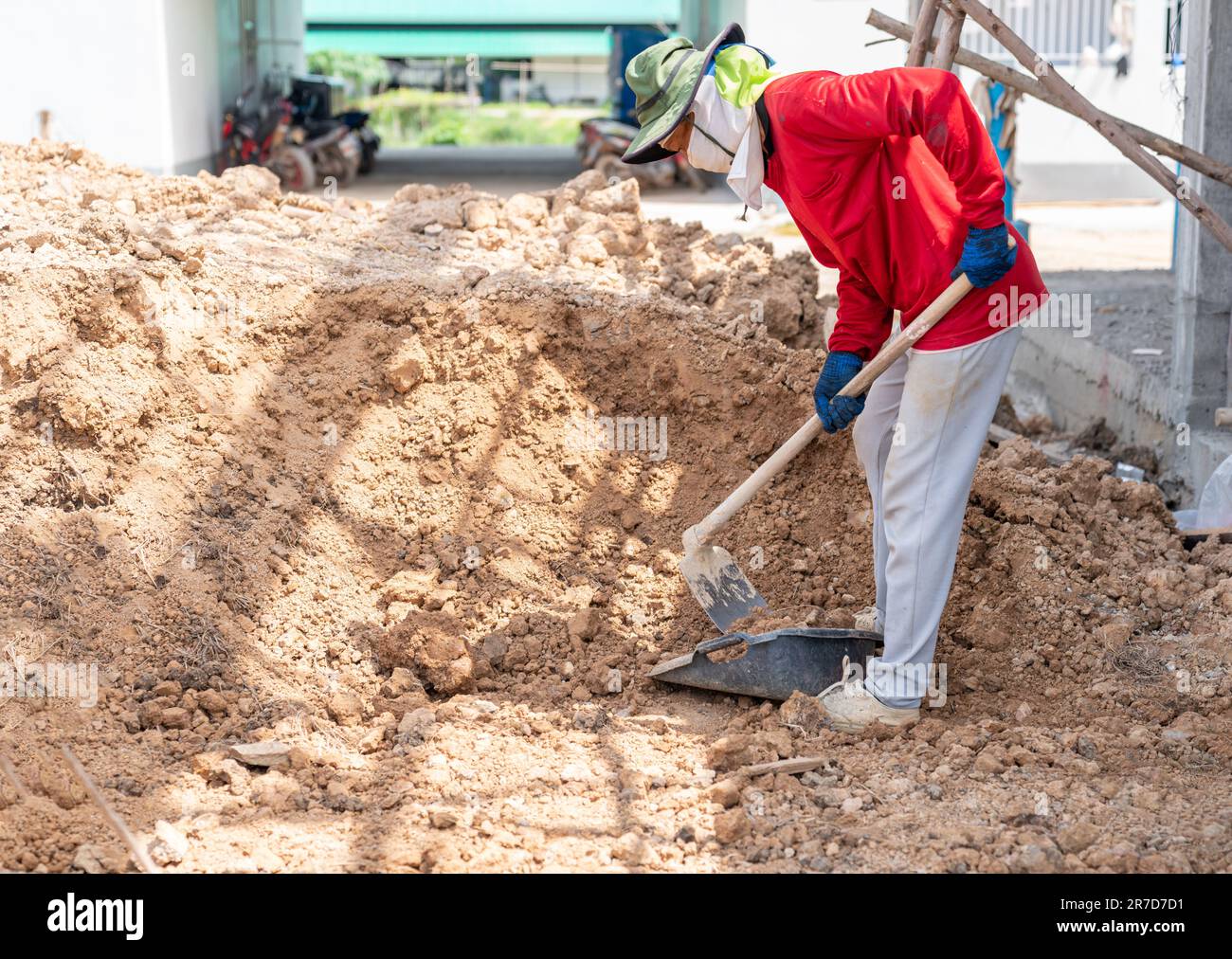 Worker with shovel loading soil in basket on building site Stock Photo ...