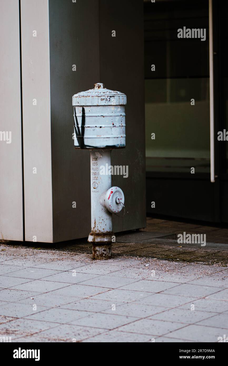 A small, red fire hydrant on the sidewalk outside of a large, urban ...