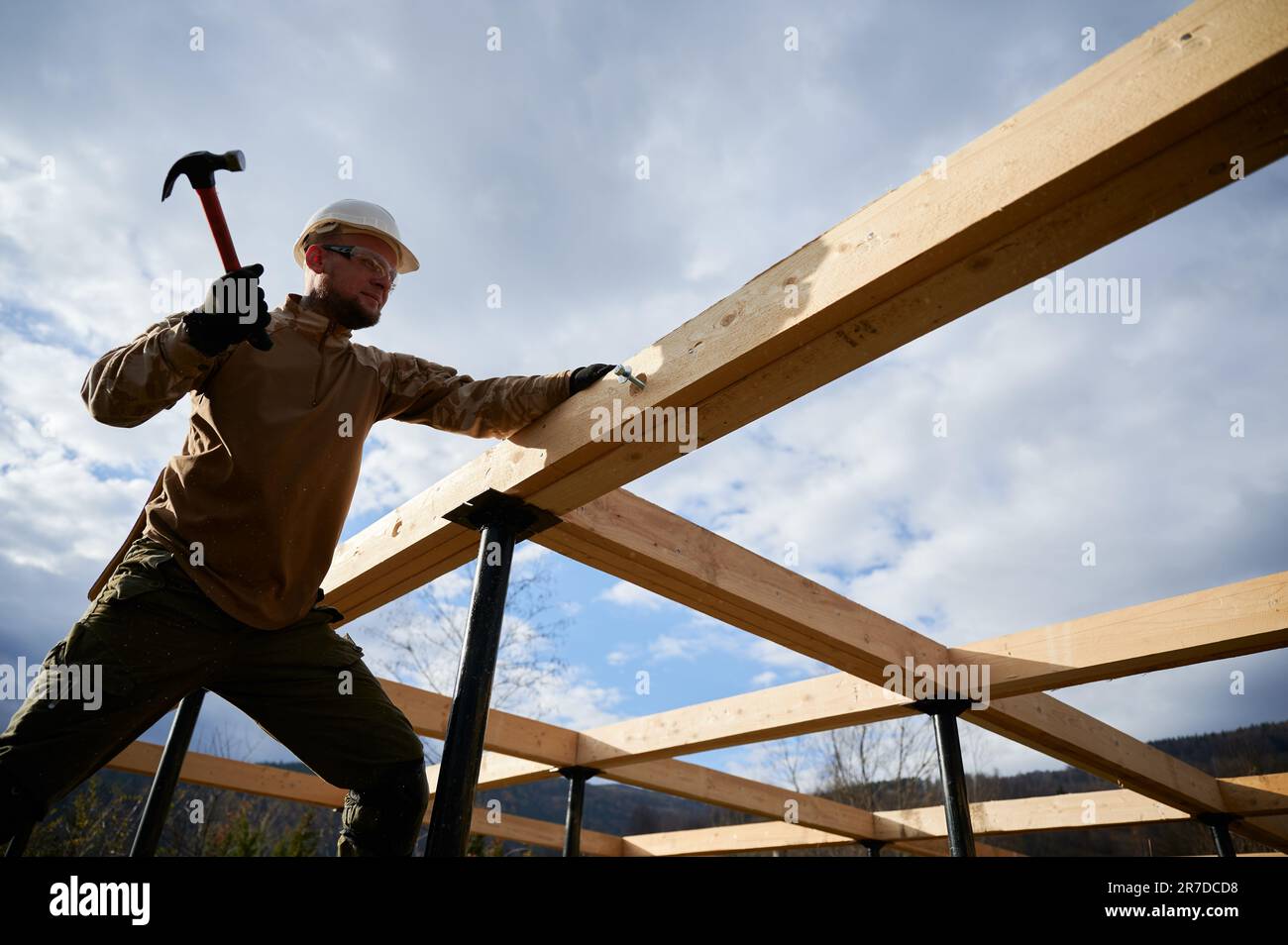 Man worker building wooden frame house on pile foundation. Carpenter ...