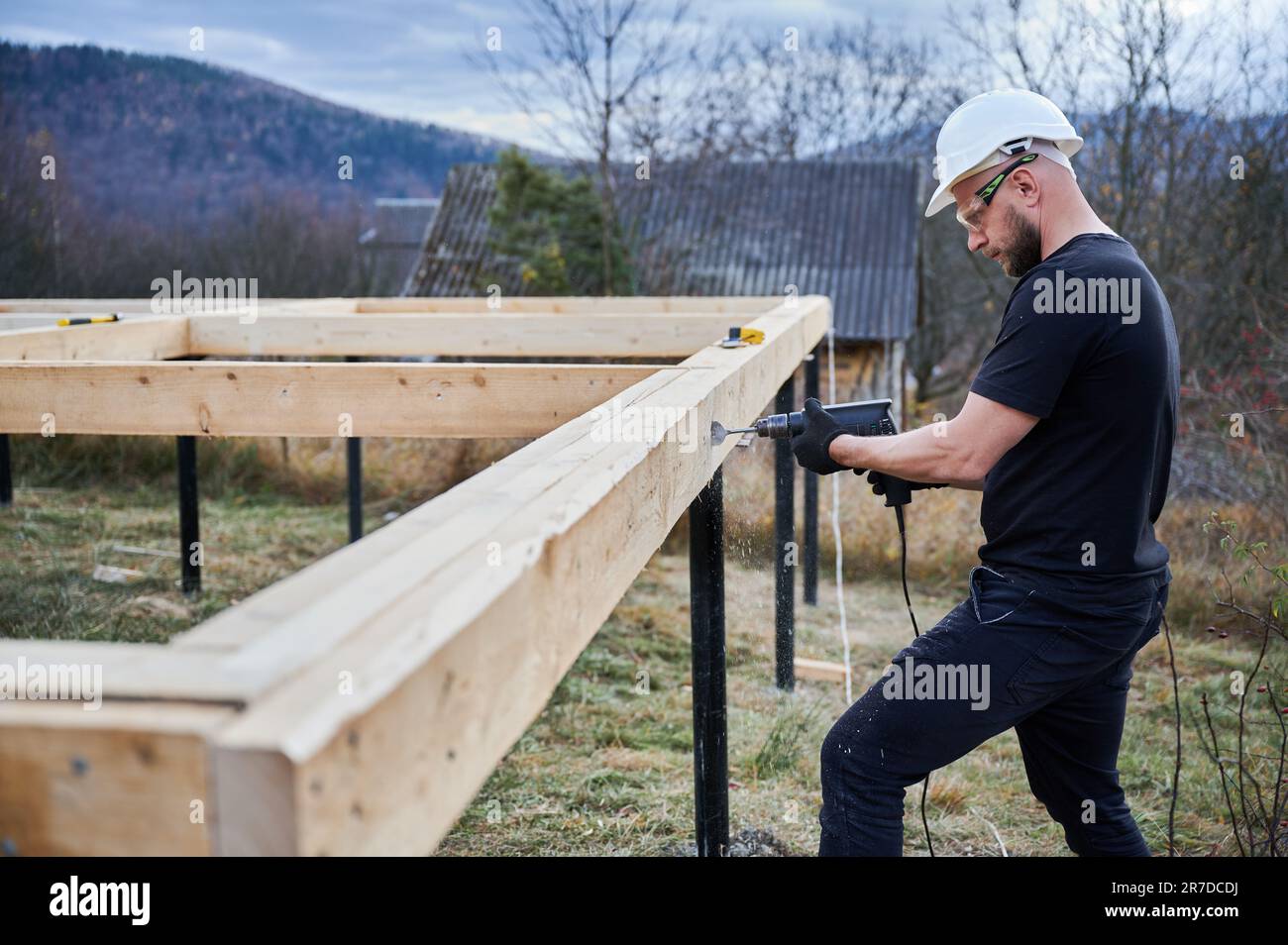 Man building wooden frame house on pile foundation. Male worker ...