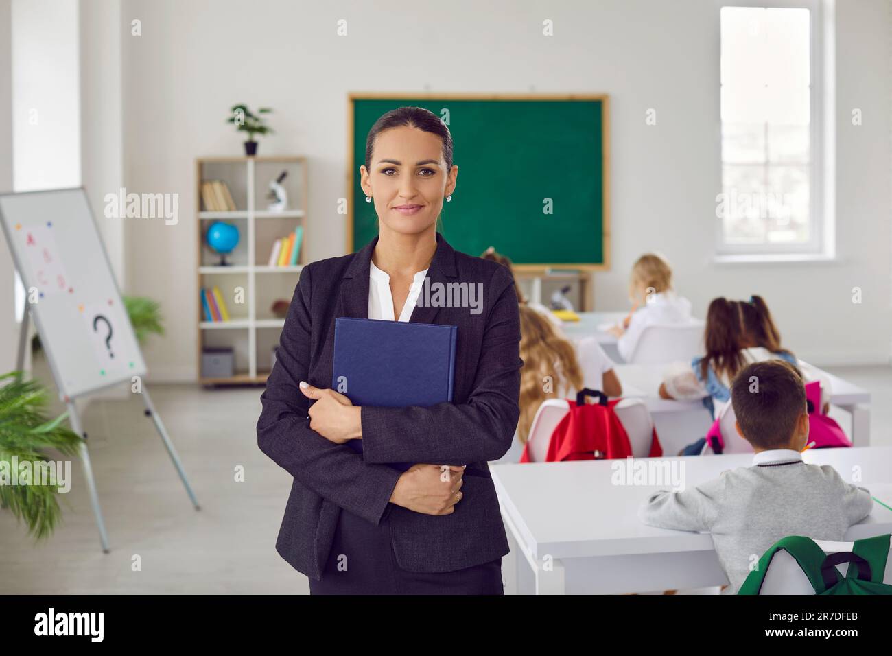 Portrait of a school teacher standing in the classroom with children in ...