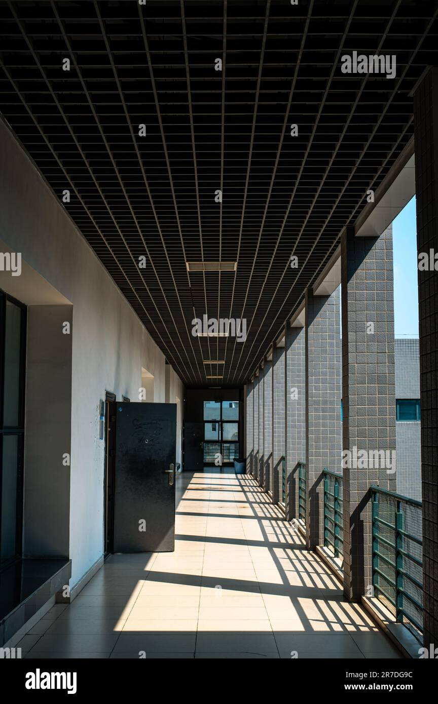 A long, narrow hallway with white walls on one side and metal railings ...