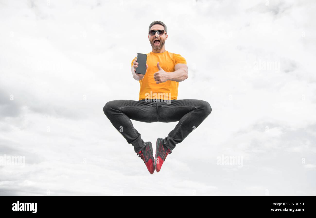man jumping and presenting smartphone on sky background. thumb up Stock ...
