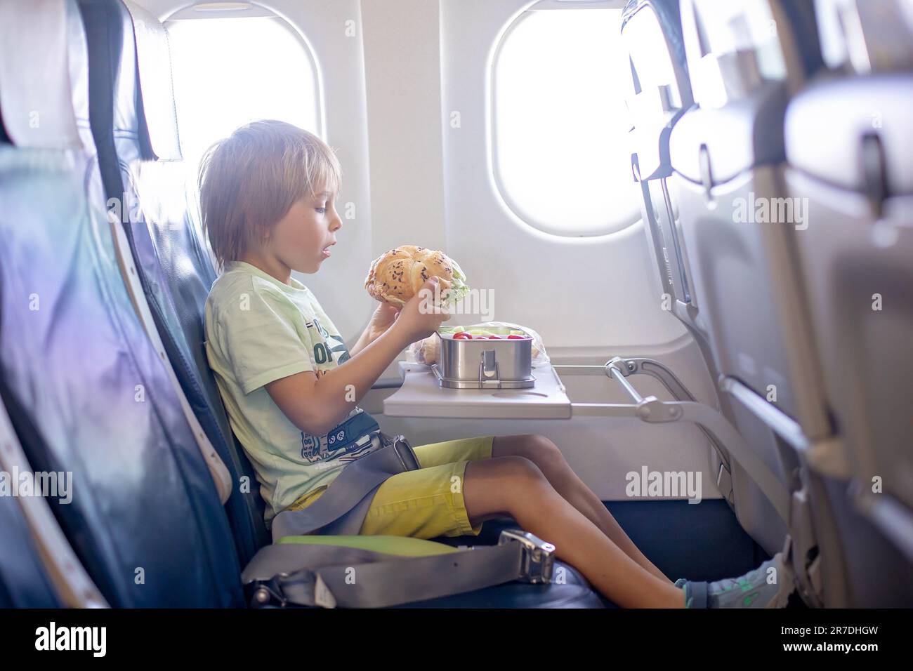 Cute preschool child, flying on a long distant flight, eating burger in ...