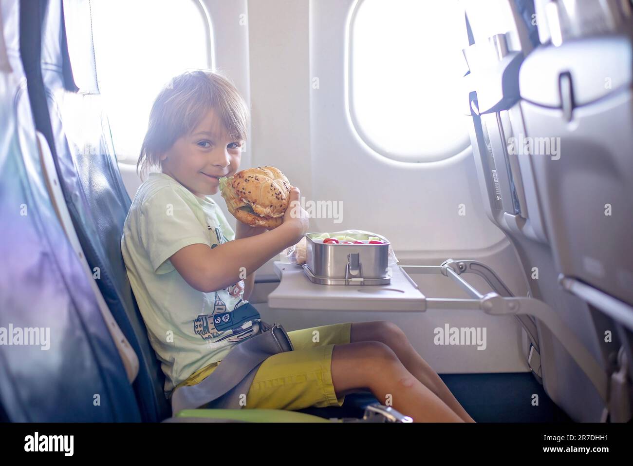 Cute preschool child, flying on a long distant flight, eating burger in ...