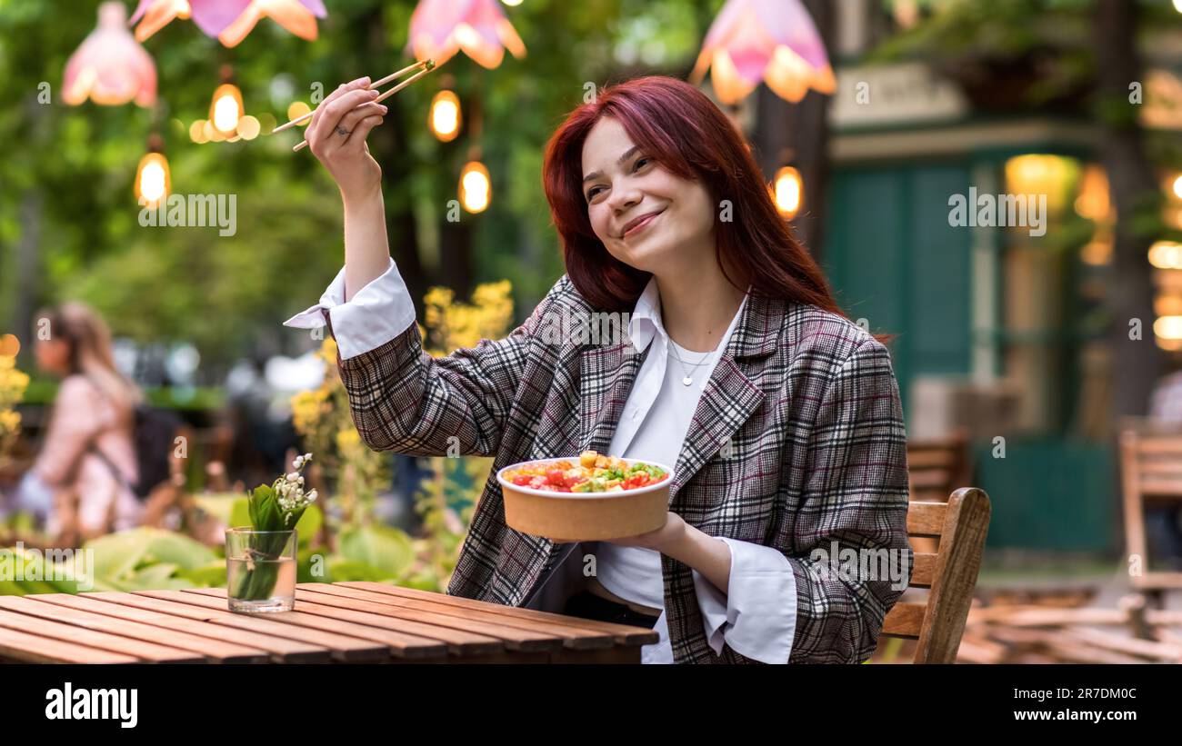 Portrait of a smiling young woman eating poke bowl with vegetables and ...