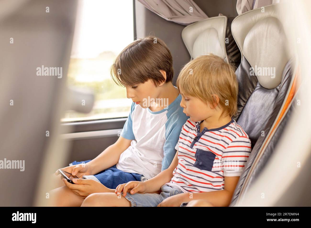 Children, siblings, playing on a mobile phone while traveling with bus ...