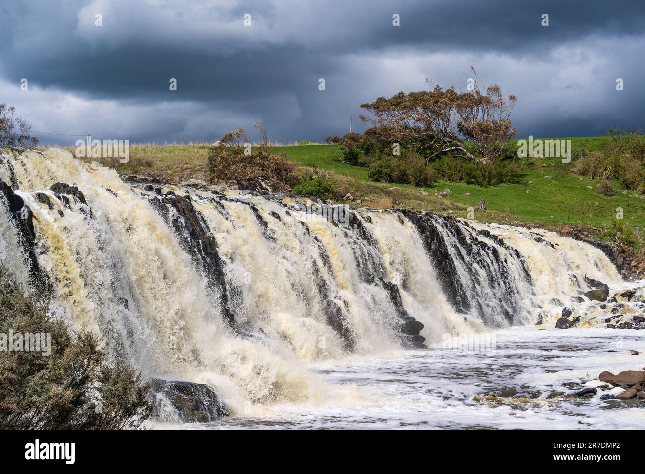 A wide flooded waterfall cascading into valley under a dark stormy sky ...