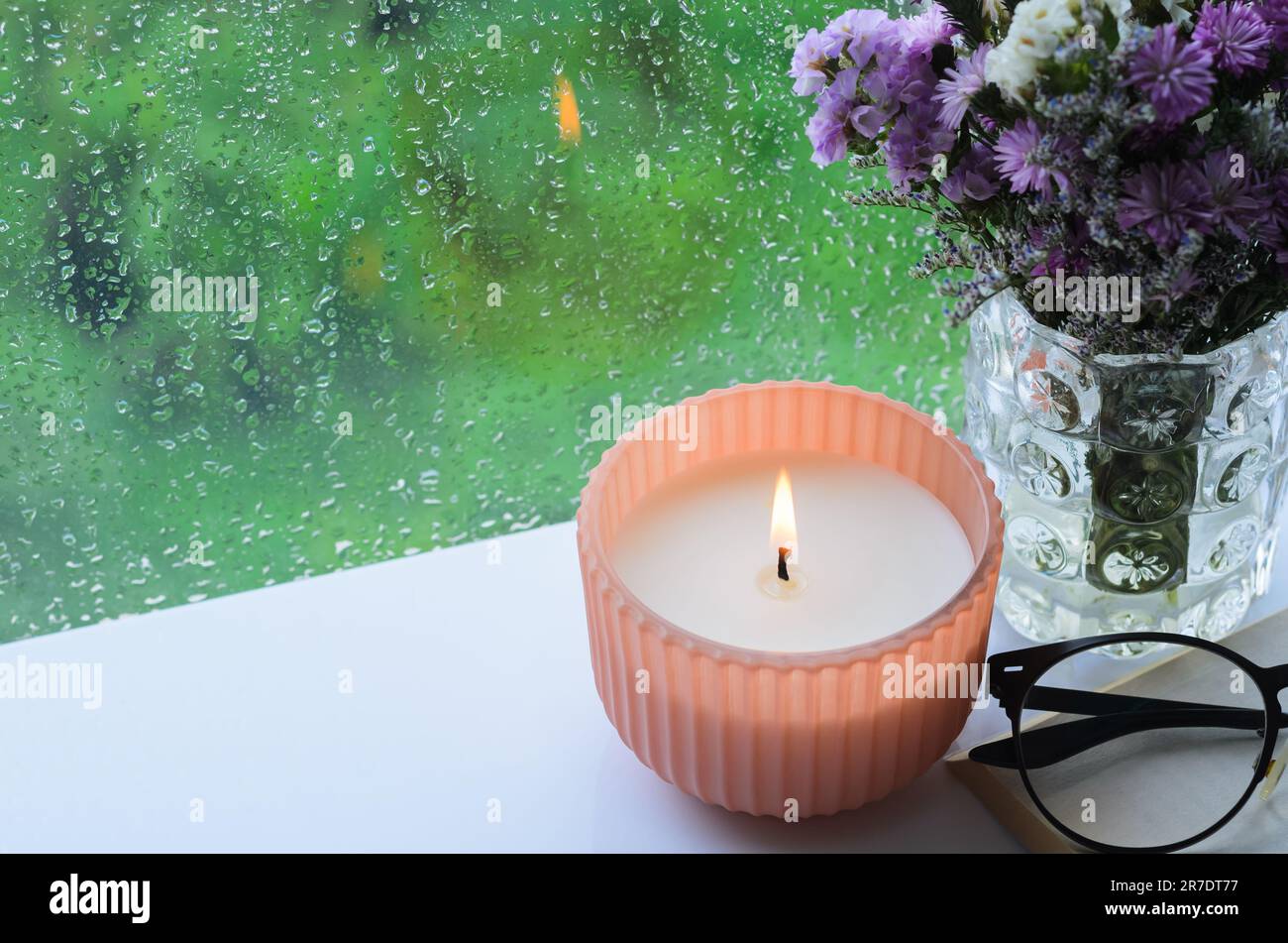 Flame burning at aroma candle puts near by window with rain drop in ...