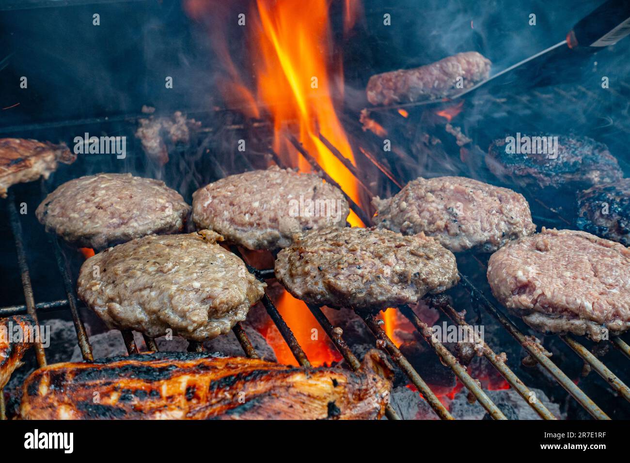 Beef burgers cooking on a barbecue with orange, red flames licking up ...