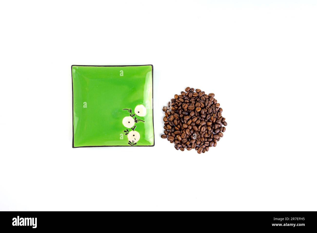 A pile of coffee beans next to a square green saucer, white background ...