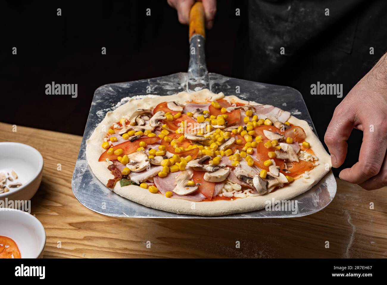A young adult male expertly adding cheese and other pizza toppings on a ...