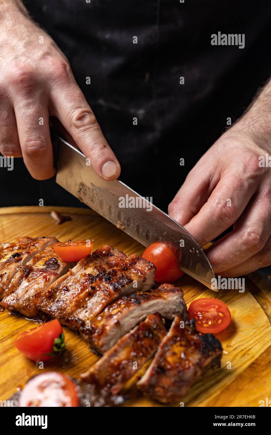 A chef wearing a black apron using a sharp kitchen knife to cut a ...
