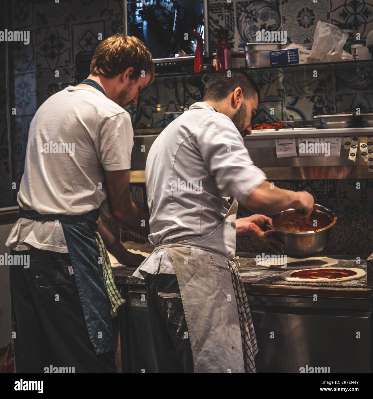 Two chefs in a kitchen preparing homemade pizza on top of a stovetop ...