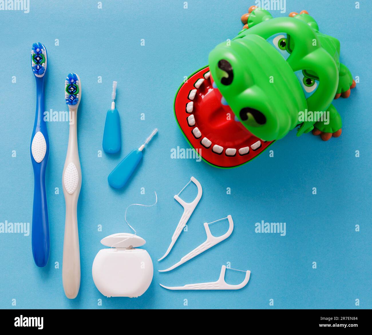 White dental floss, toothpicks, brushes and crocodile on blue ...