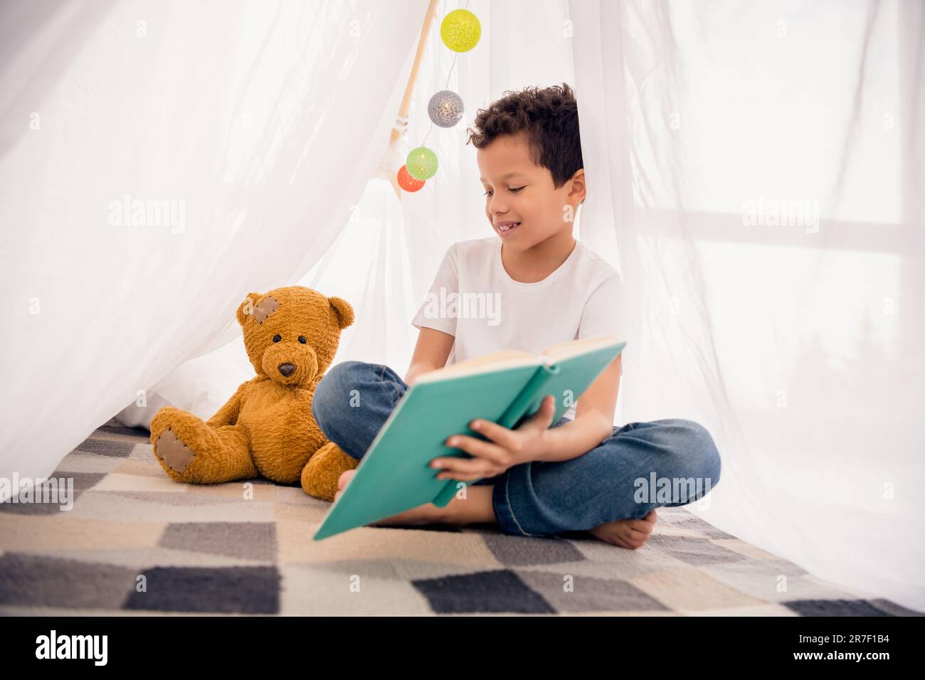 Photo of smart schoolkid reading book telling story teddy bear in ...