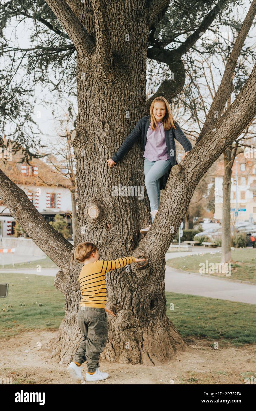 Two funny kids playing outside in spring park, climbing the tree ...