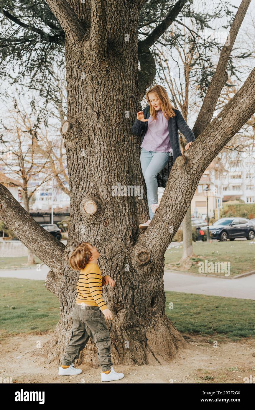 Two funny kids playing outside in spring park, climbing the tree ...