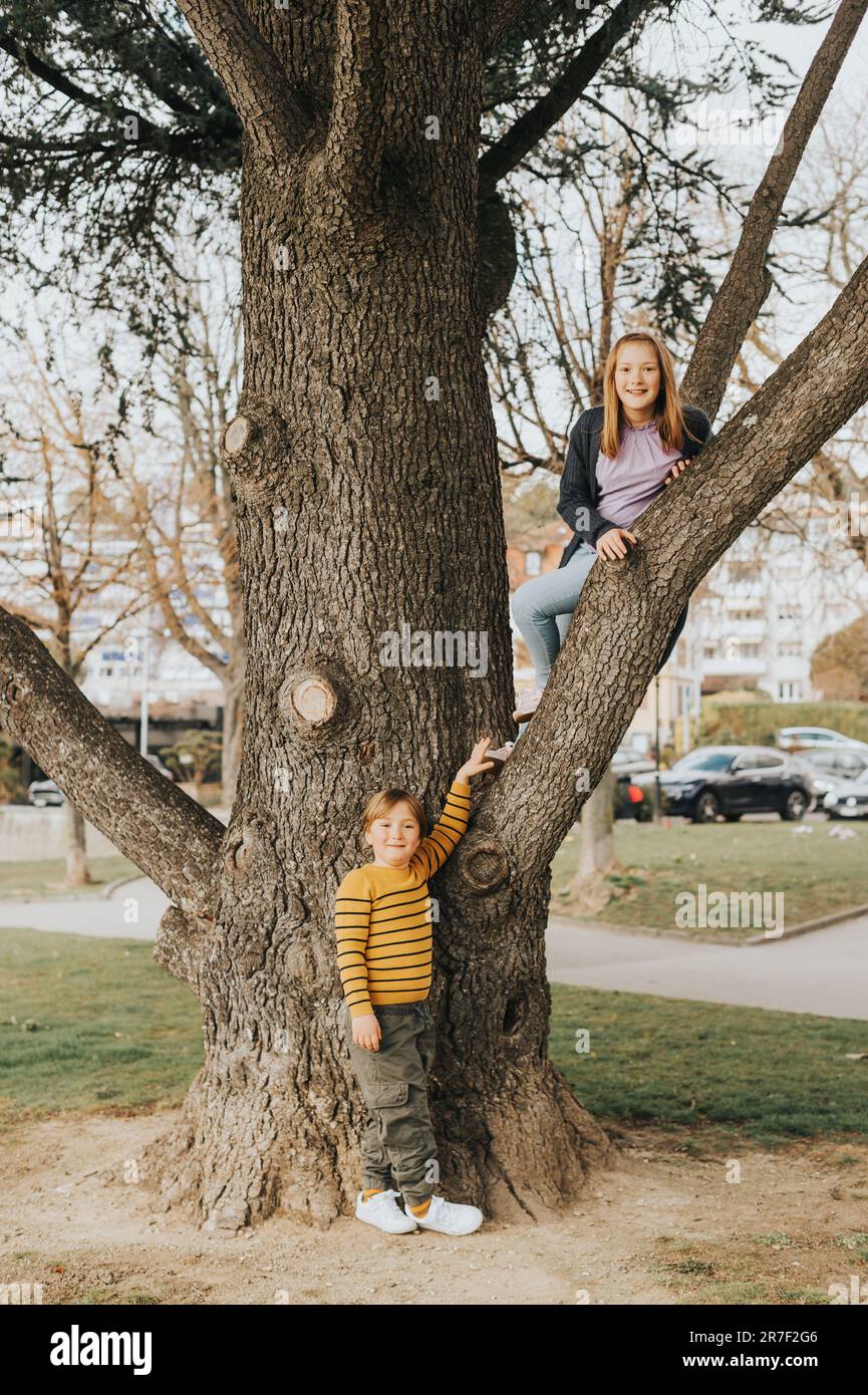 Two funny kids playing outside in spring park, climbing the tree ...