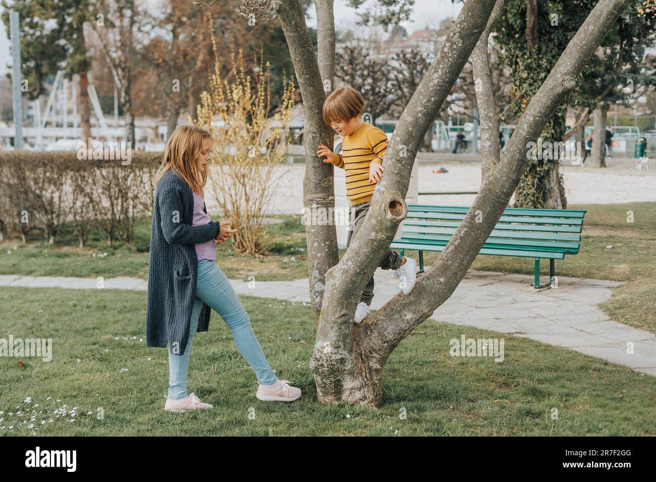 Two funny kids playing outside in spring park, climbing the tree ...