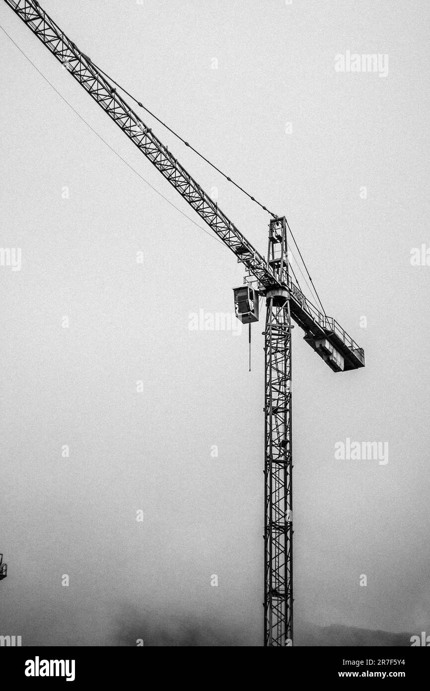 A large construction crane positioned next to an airplane in the misty ...