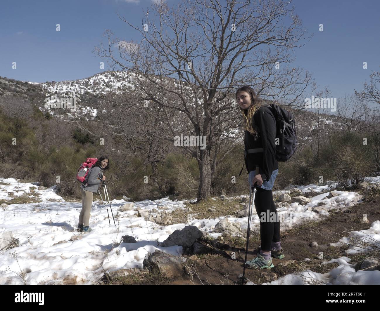 two girls sisters are hiking in the snow with backpack and walking ...