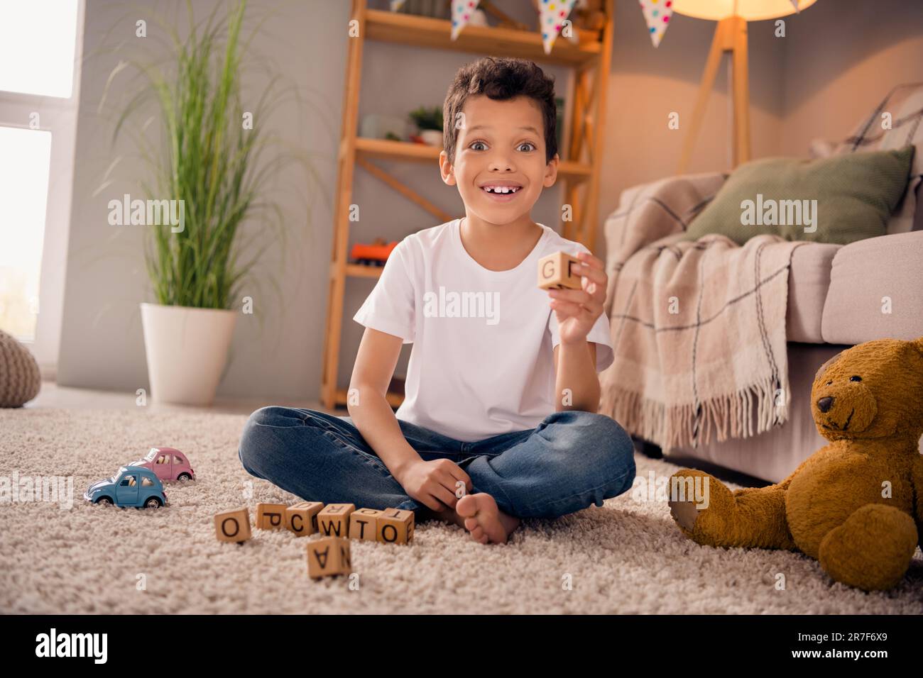Photo of surprised preschool boy sit floor playroom show abc block with ...