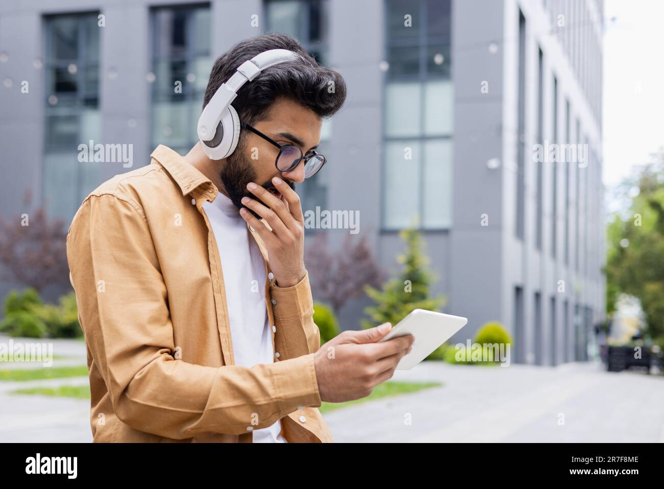 Young man with headphones and tablet computer sitting outside office ...