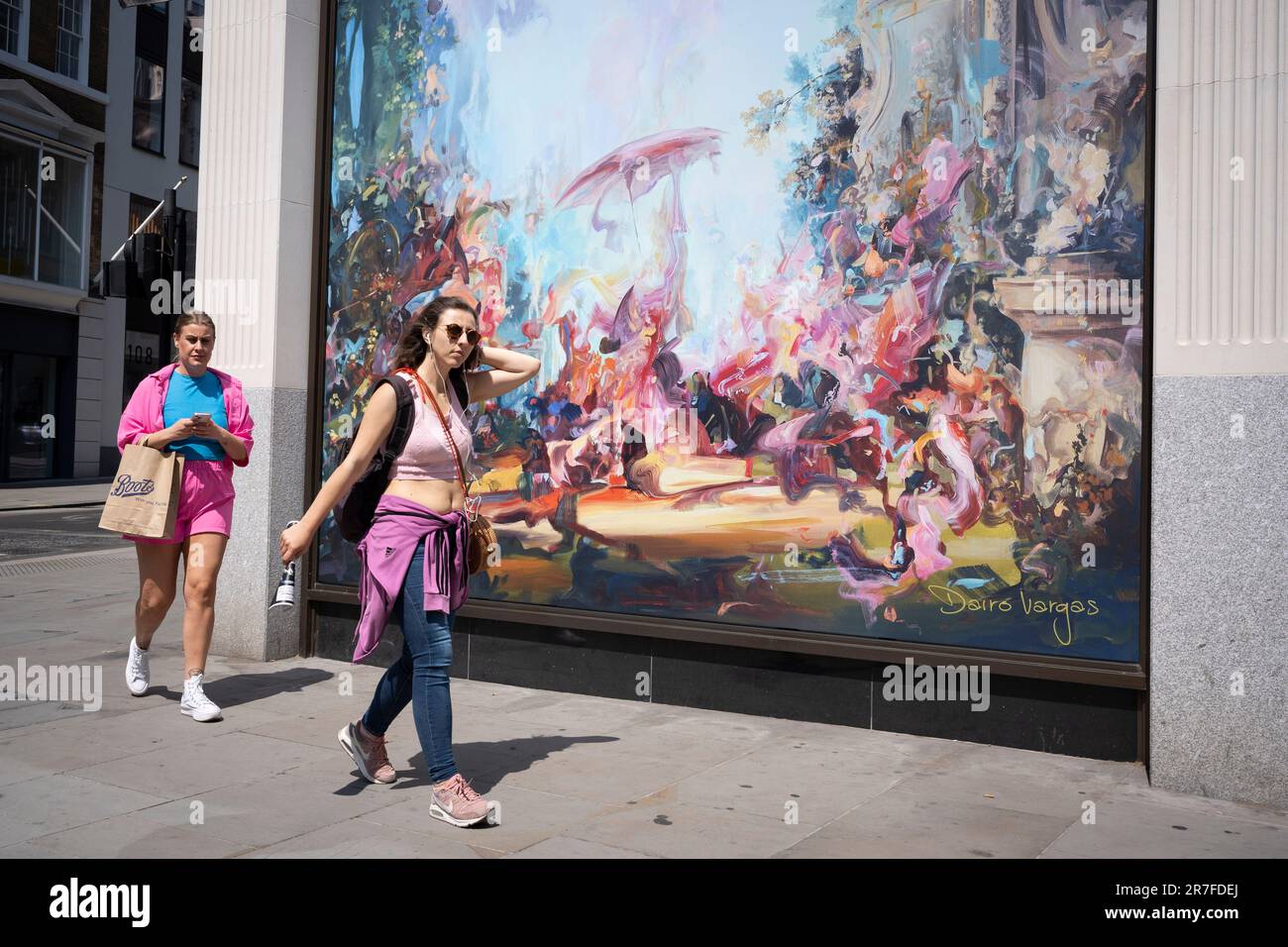 Two women wearing shades of pinks walk past a construction hoarding ...