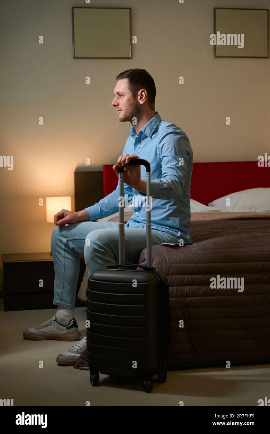 Handsome guy looking in window sitting on bed in hotel room Stock Photo ...
