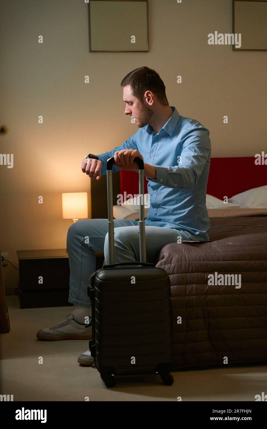 Man looking at clock sitting on bed in hotel room Stock Photo - Alamy