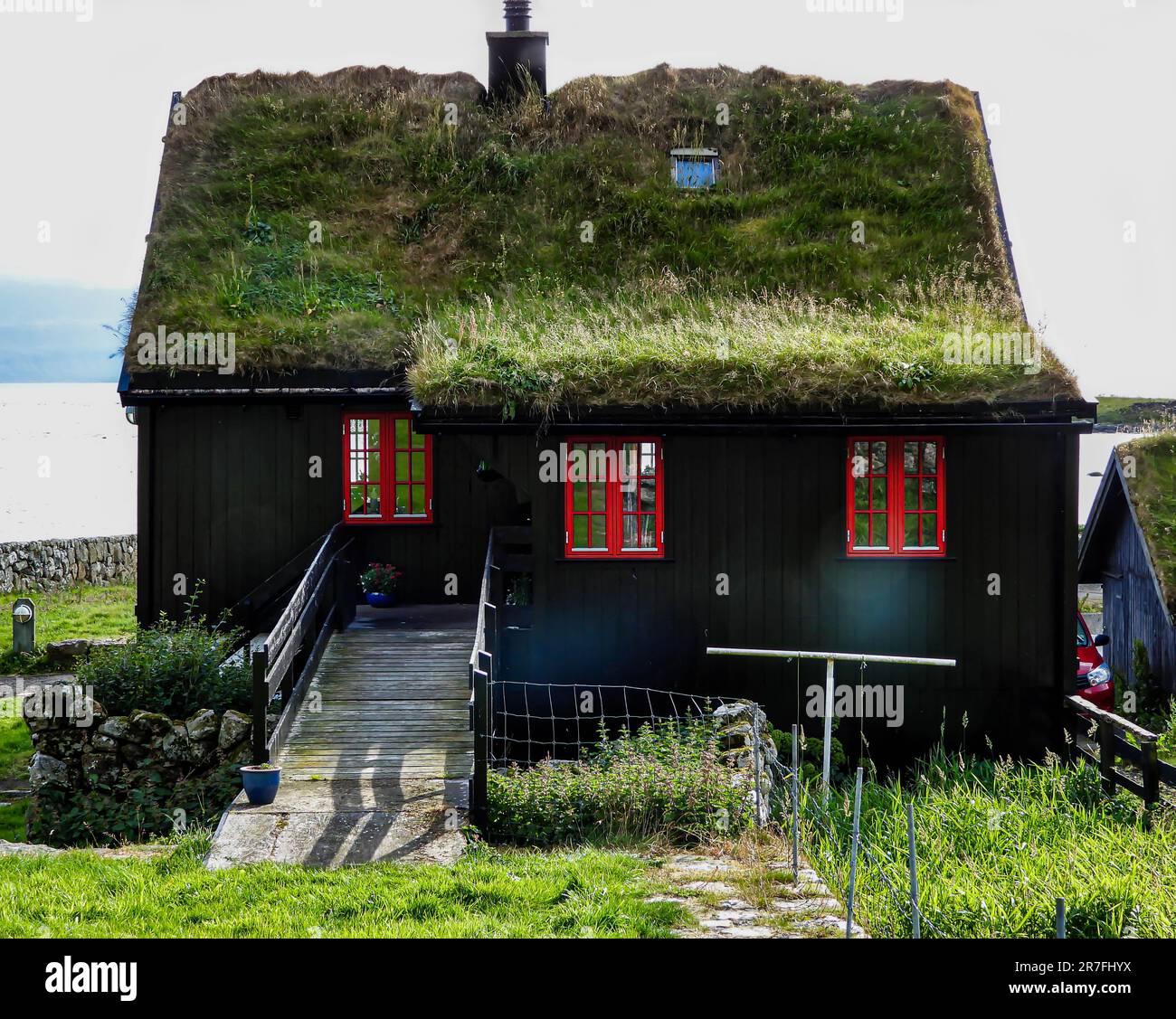 A charming rural cottage featuring a grass-thatched roof and red window ...