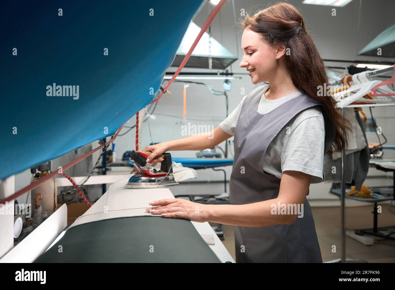 Dry cleaner service worker ironing cloth after pressing on steam board ...