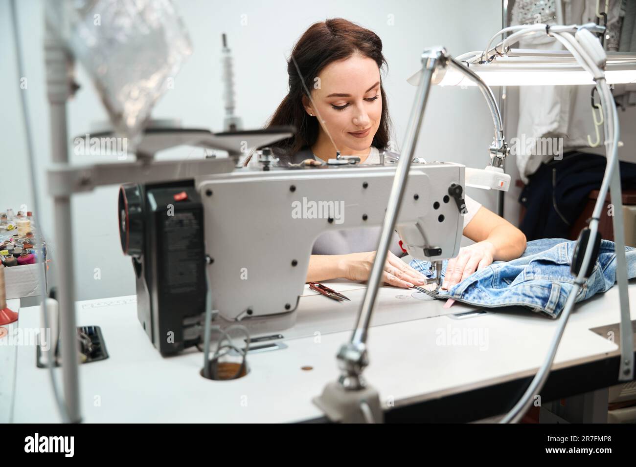 Needlewoman sewing tags and processing clothes on sewing machine Stock ...