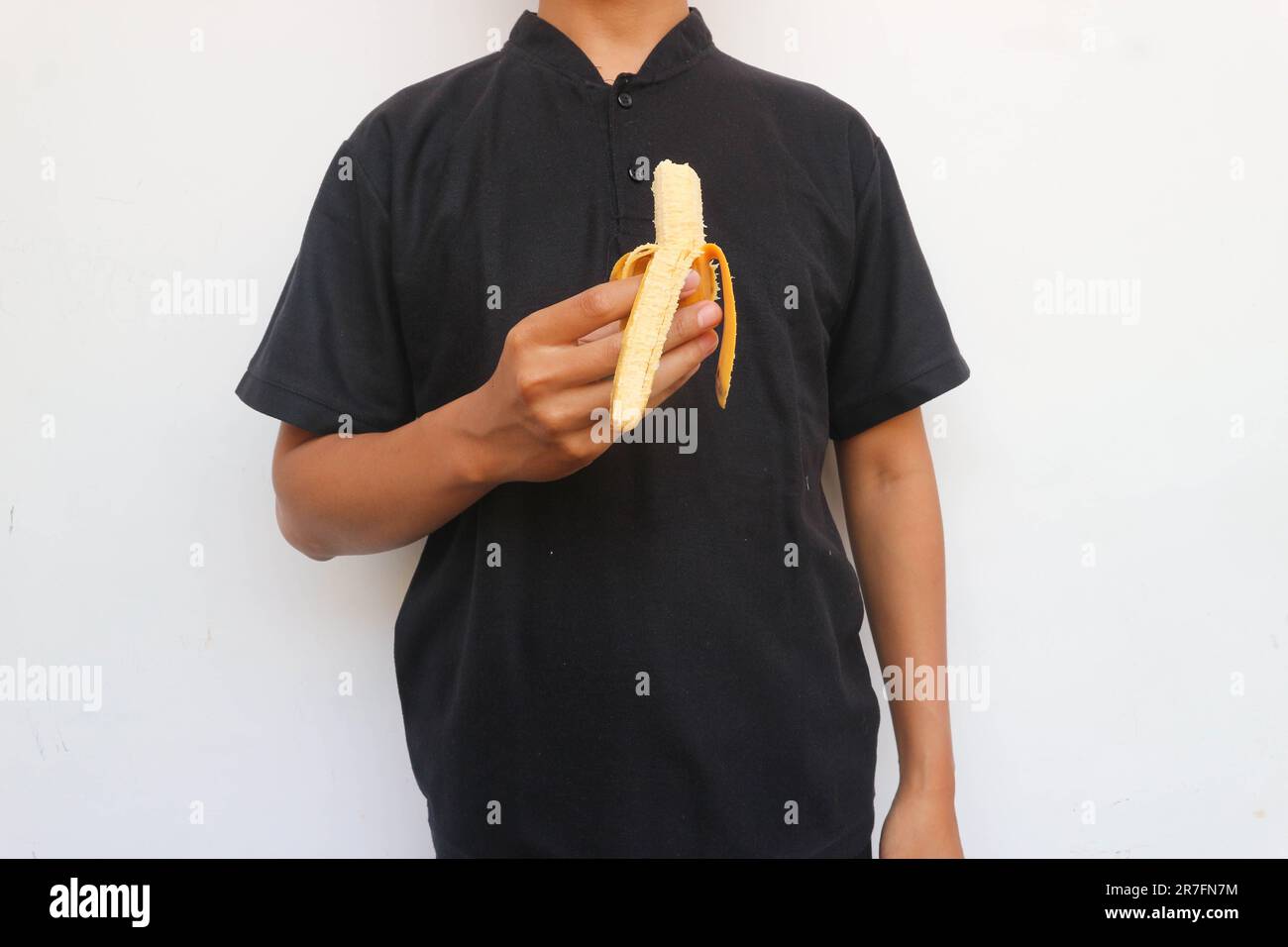 The man in black shirt is standing while holding a banana Stock Photo ...