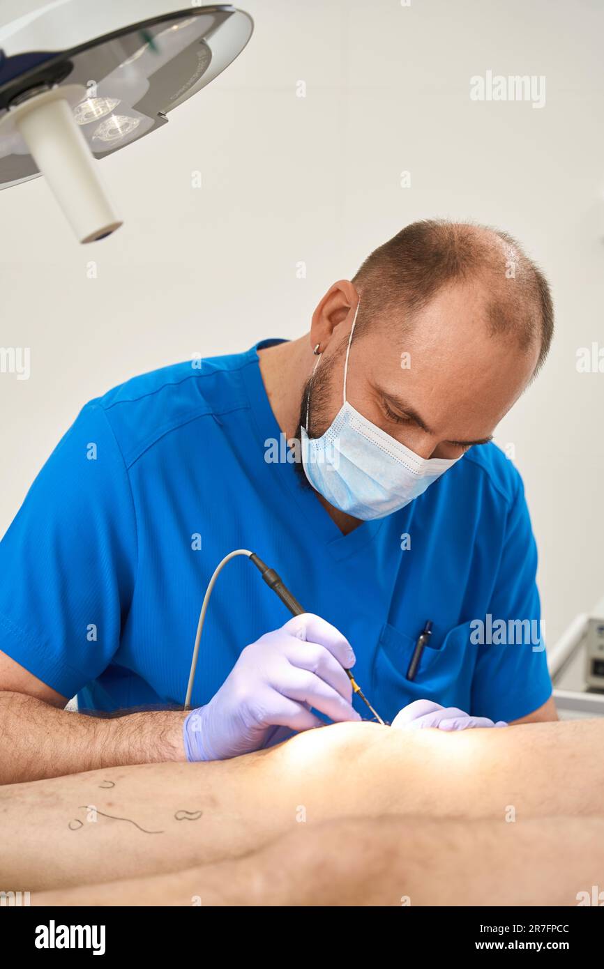 Focused male surgeon performs surgery on patient leg using ...