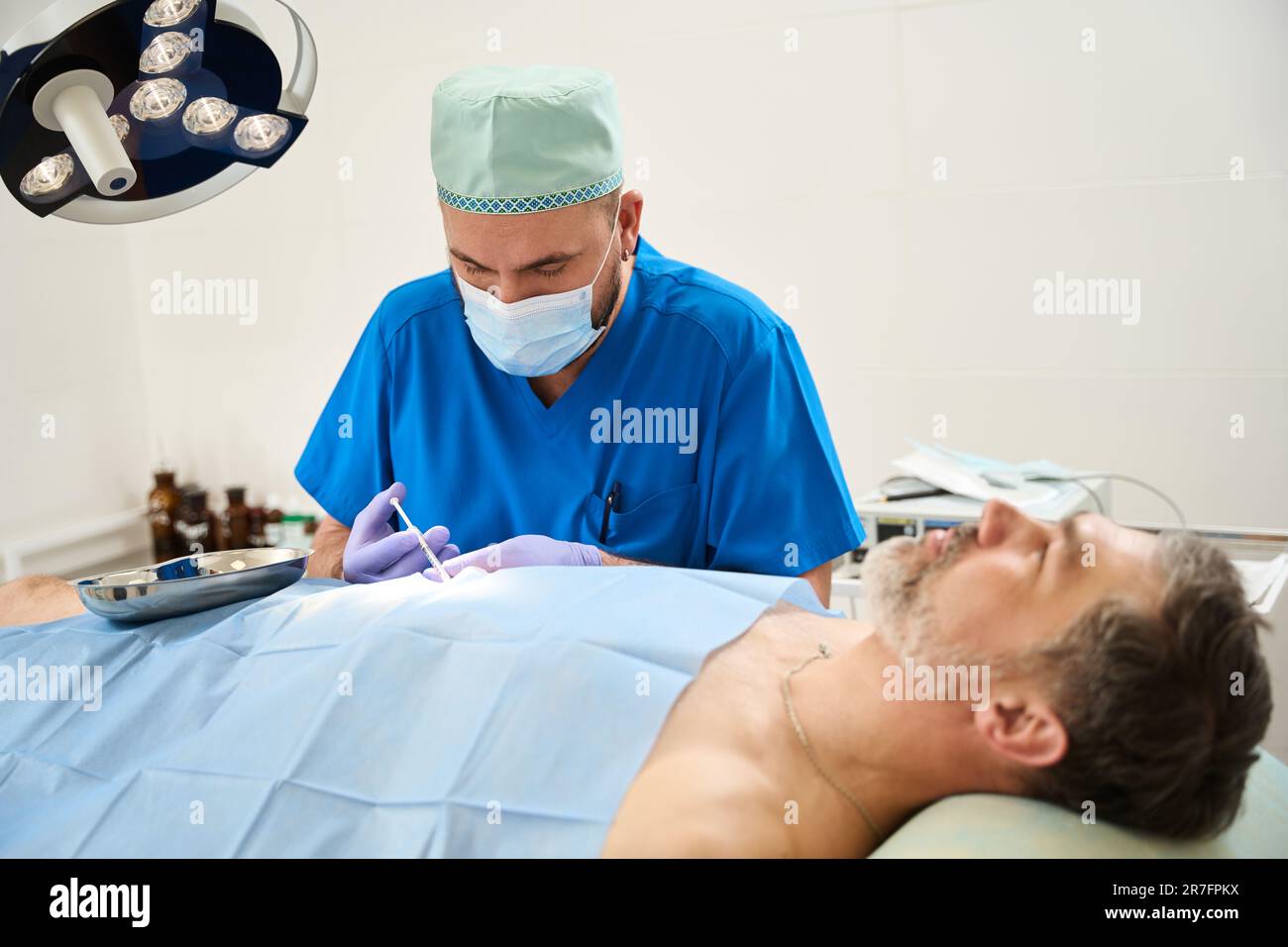 Surgeon injecting syringe into elderly male patient during surgical ...